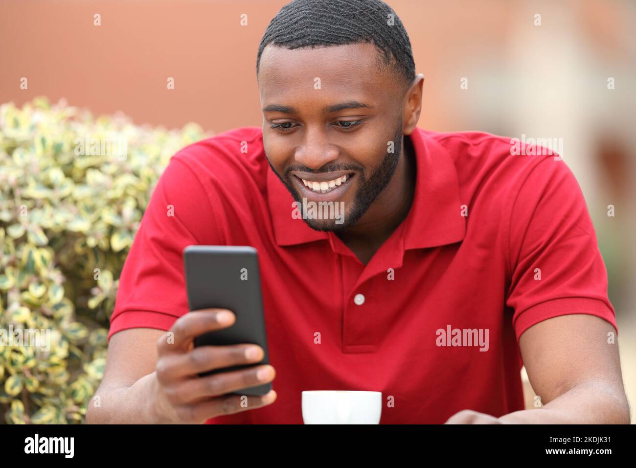 Happy black man checks cell phone sitting in a bar terrace Stock Photo ...