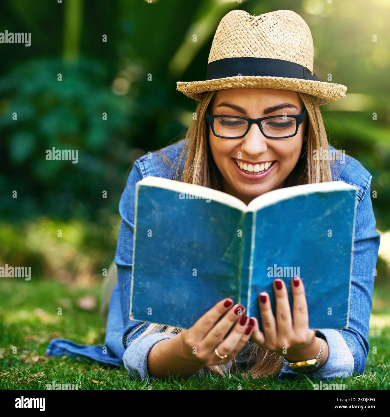 Getting lost in her favourite book. an attractive young woman reading a book while lying outside ...