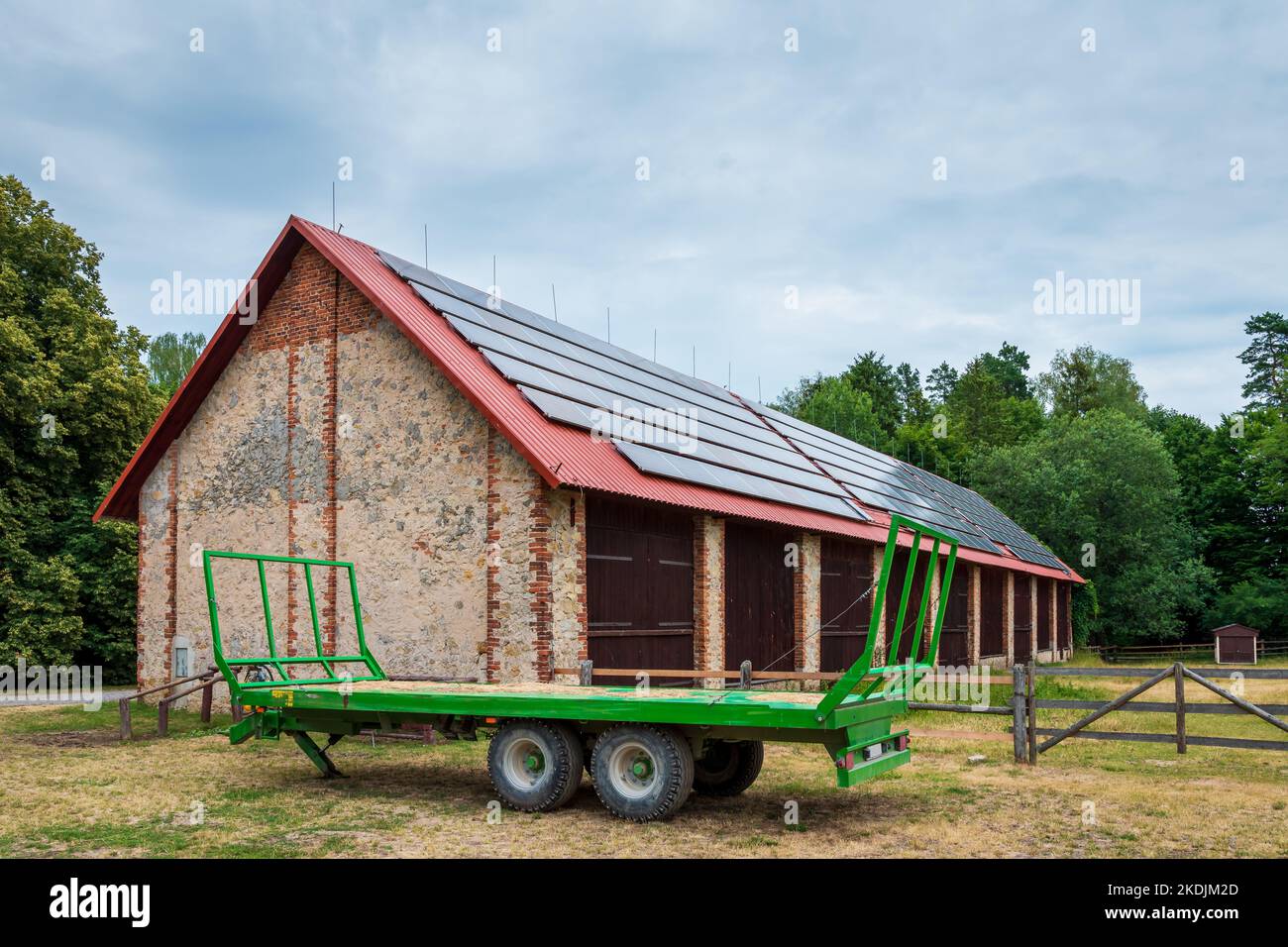 Green farm trailer parked in front of a large barn. Solar panels ...