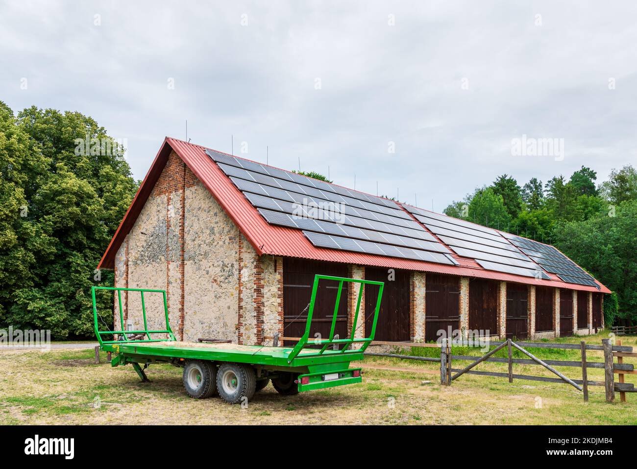 Green farm trailer parked in front of a large barn. Solar panels ...