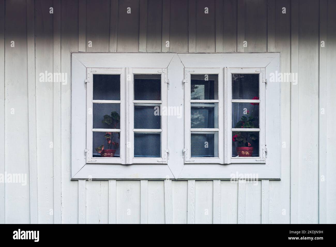 A detail of a white window against a white facade made of wooden planks ...