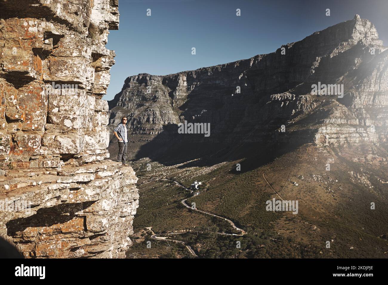 What a view. a young man standing on the edge of a mountain cliff ...