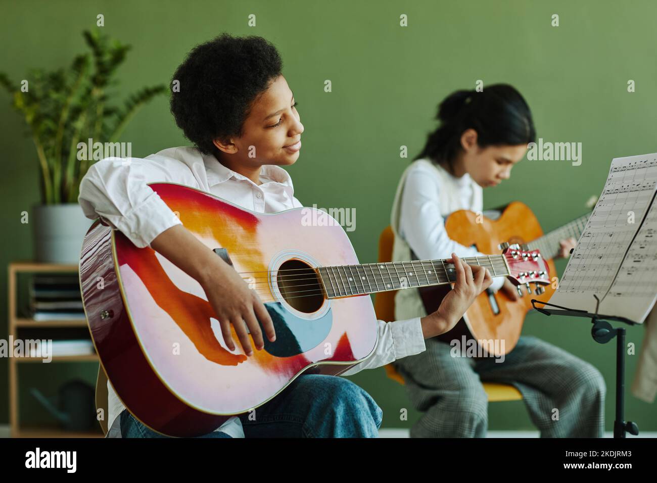 Diligent African American schoolgirl with acoustic guitar looking at ...