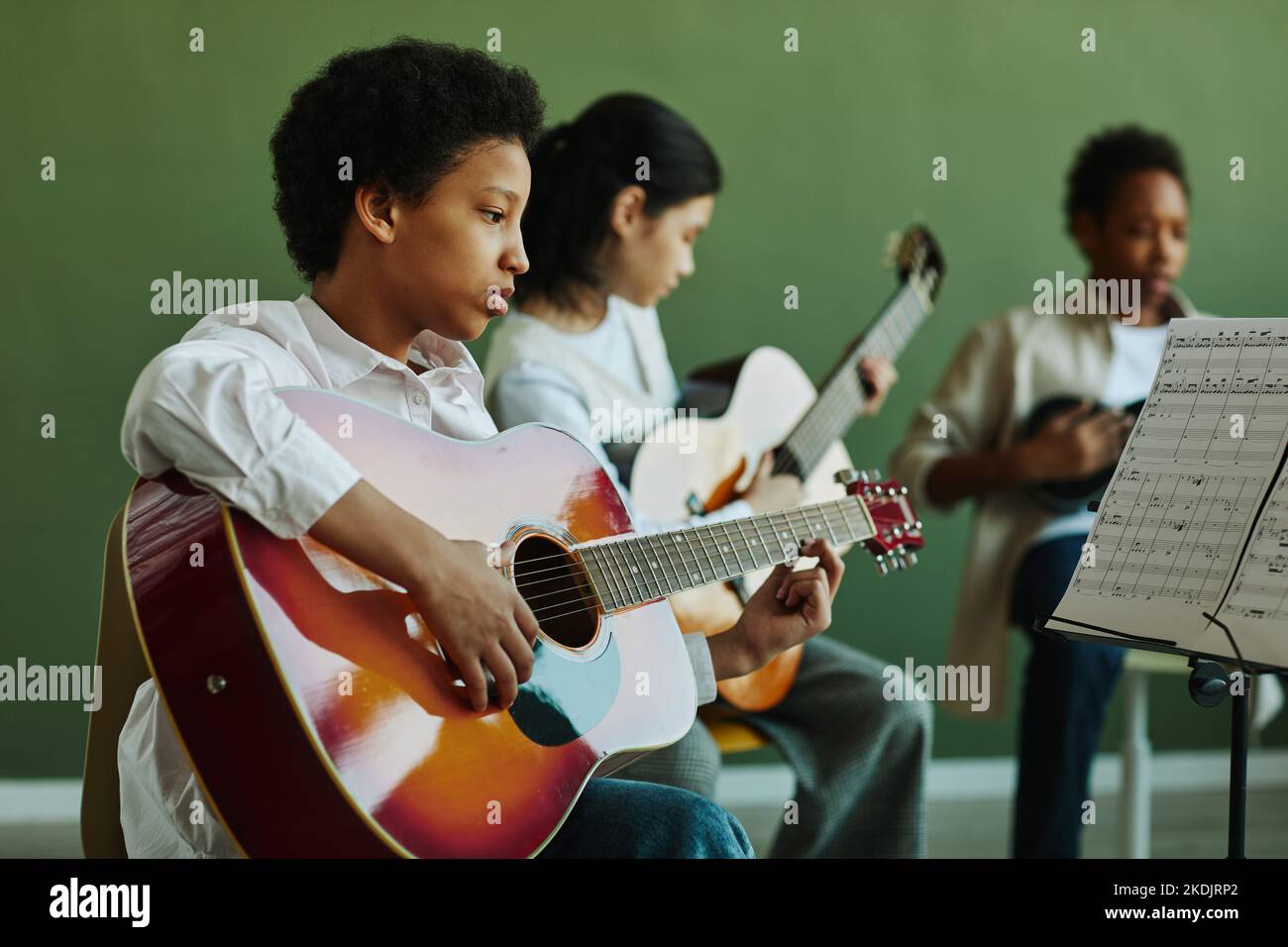 African American schoolgirl with acoustic guitar looking at paper with ...
