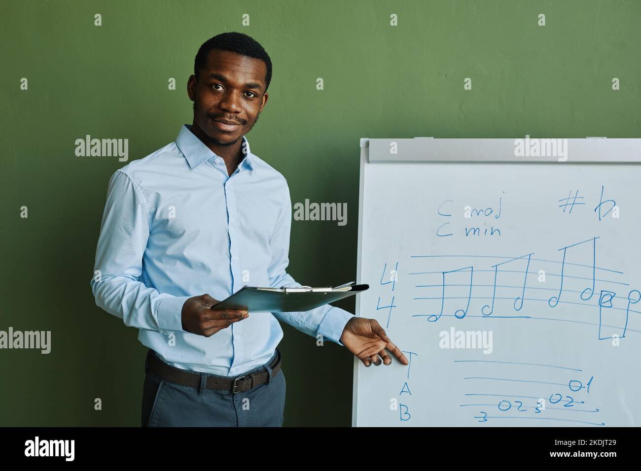 Young successful teacher of music with document pointing at whiteboard ...