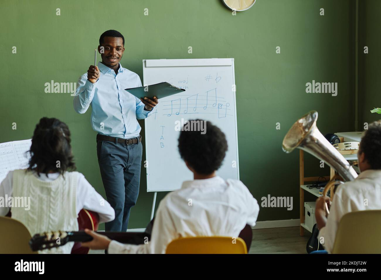 Happy young teacher of music standing by whiteboard and explaining ...