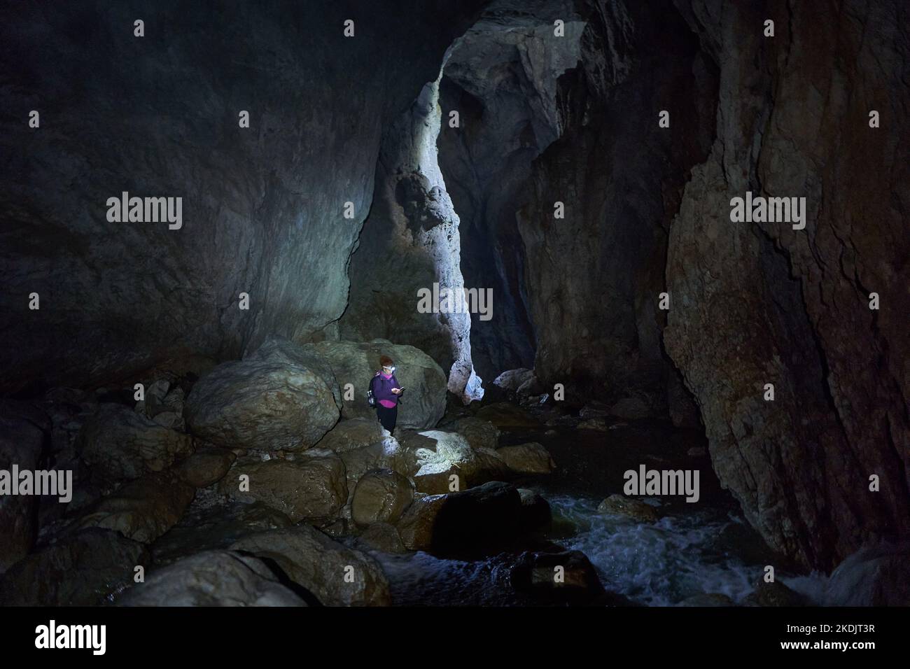 Woman with backpack hiking into a cave with a river Stock Photo - Alamy