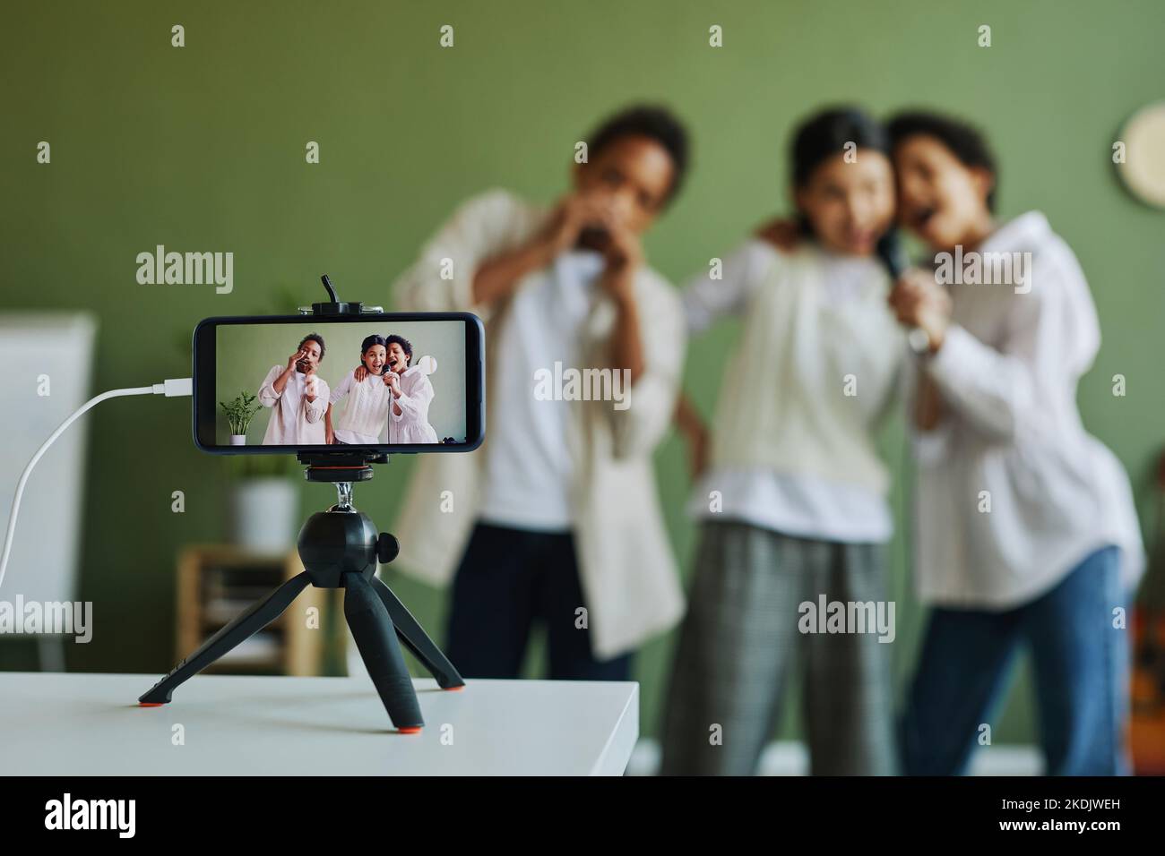 Screen of smartphone on tripod with three schoolkids performing song ...