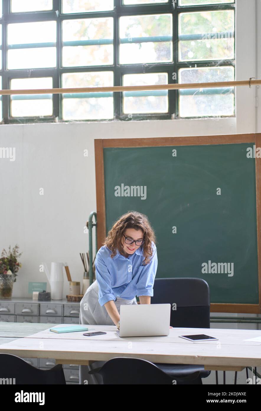 Young woman school teacher or employee standing at desk using laptop ...