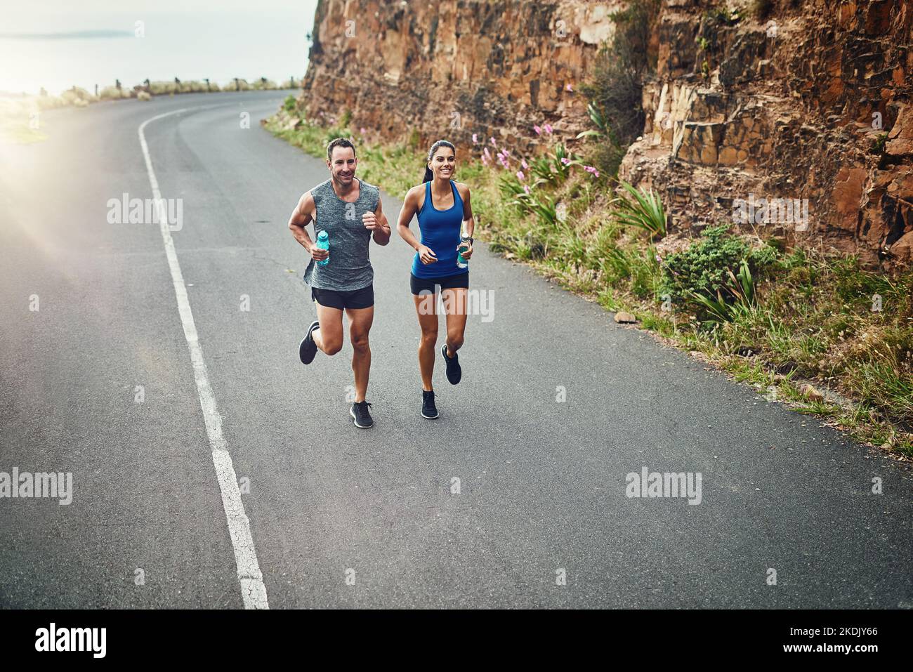 Enjoying the long road by running on it. a young attractive couple ...