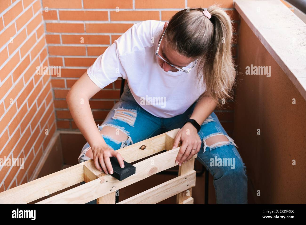 Close-up of a blonde woman sanding a pallet on the terrace with hand ...