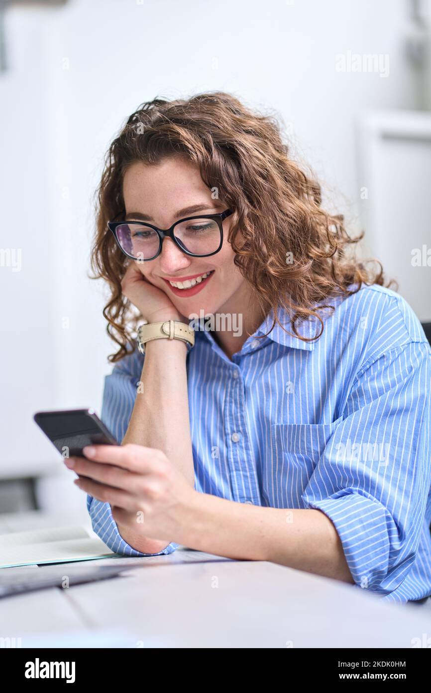 Happy young business woman using cell phone working in office, vertical ...