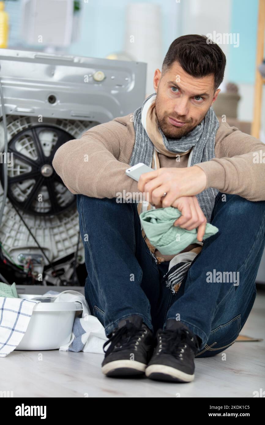 dismayed man sat next to broken washing-machine Stock Photo - Alamy