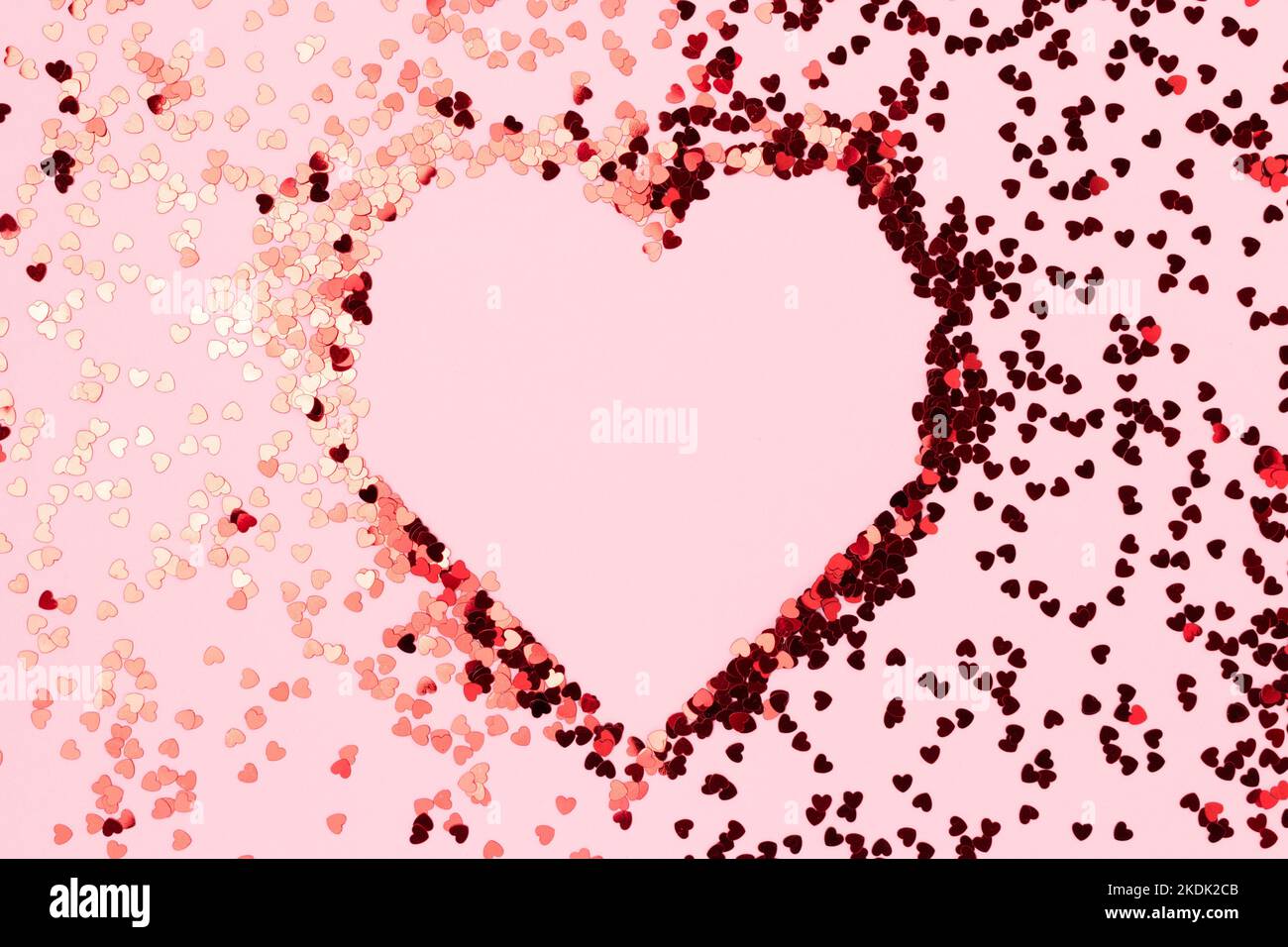 Heart shaped frame made of metallic red confetti on a pink background ...