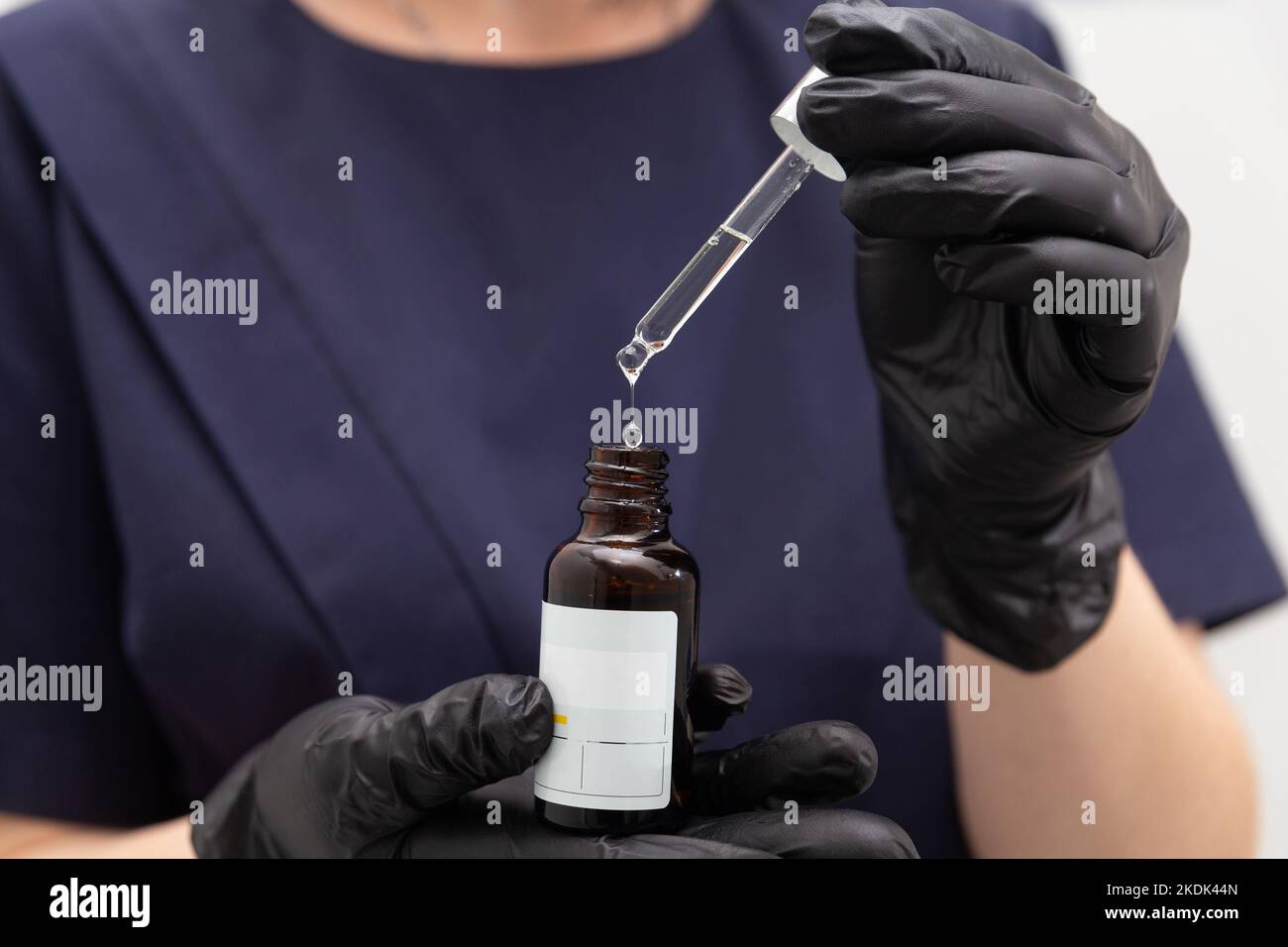 Woman hand in black medical gloves holding pipette dropper with drop of ...