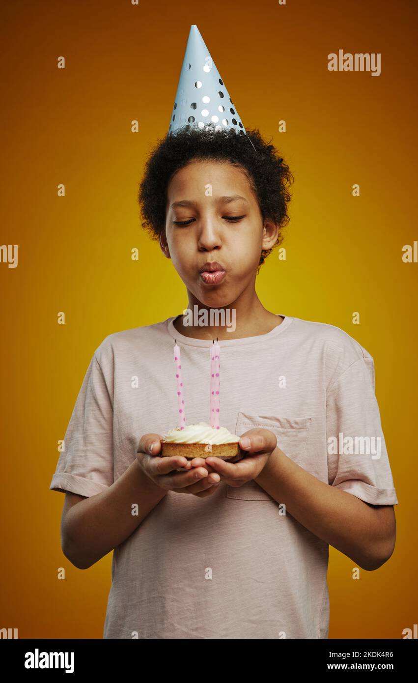 Youthful girl in birthday cap blowing candles on small homemade cake ...