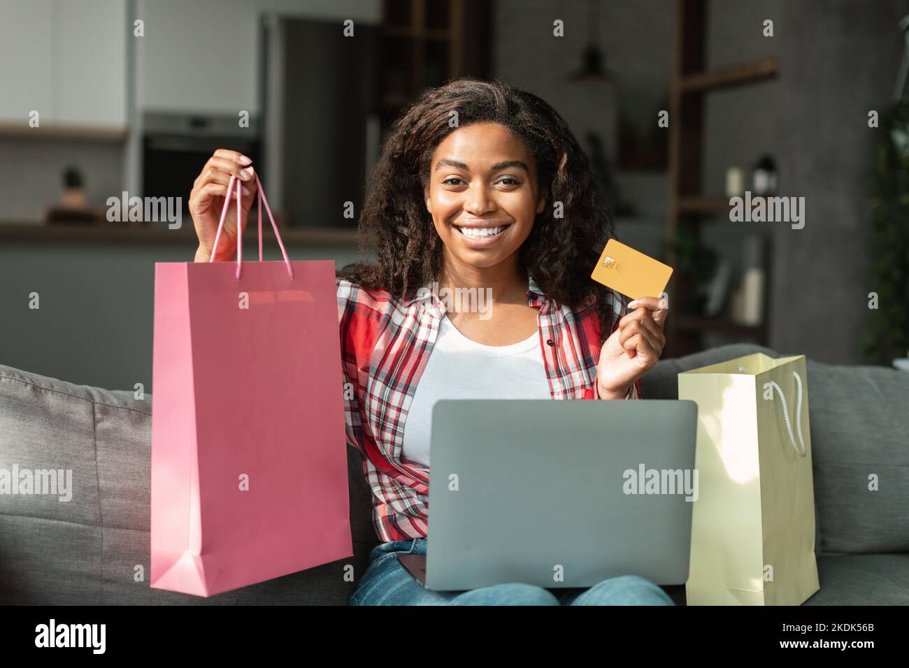 Smiling black young woman with laptop shows credit card and bag with ...
