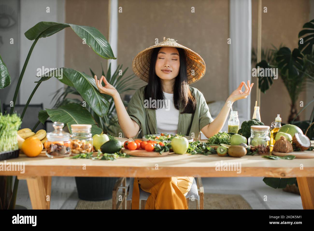 Young asian woman sitting near table with organic vegetables in yoga ...