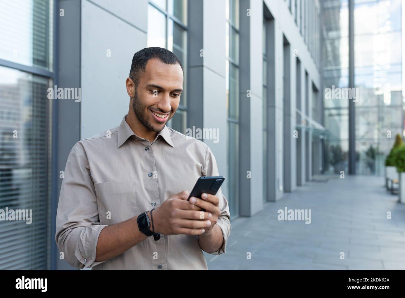 hispanic man outside modern office building using smartphone ...