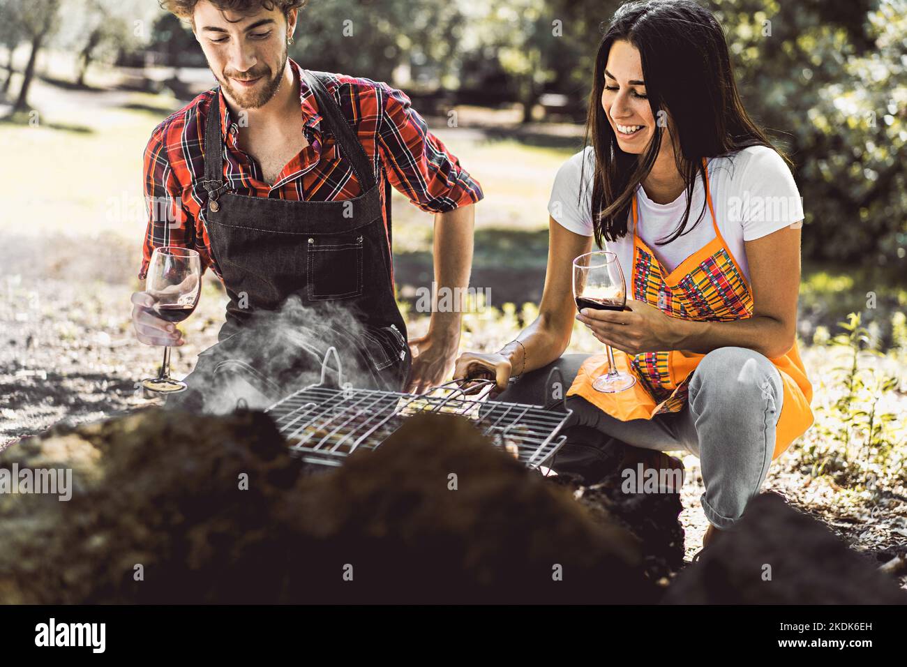 A couple of young friends at the picnic in the countryside cook grilled ...