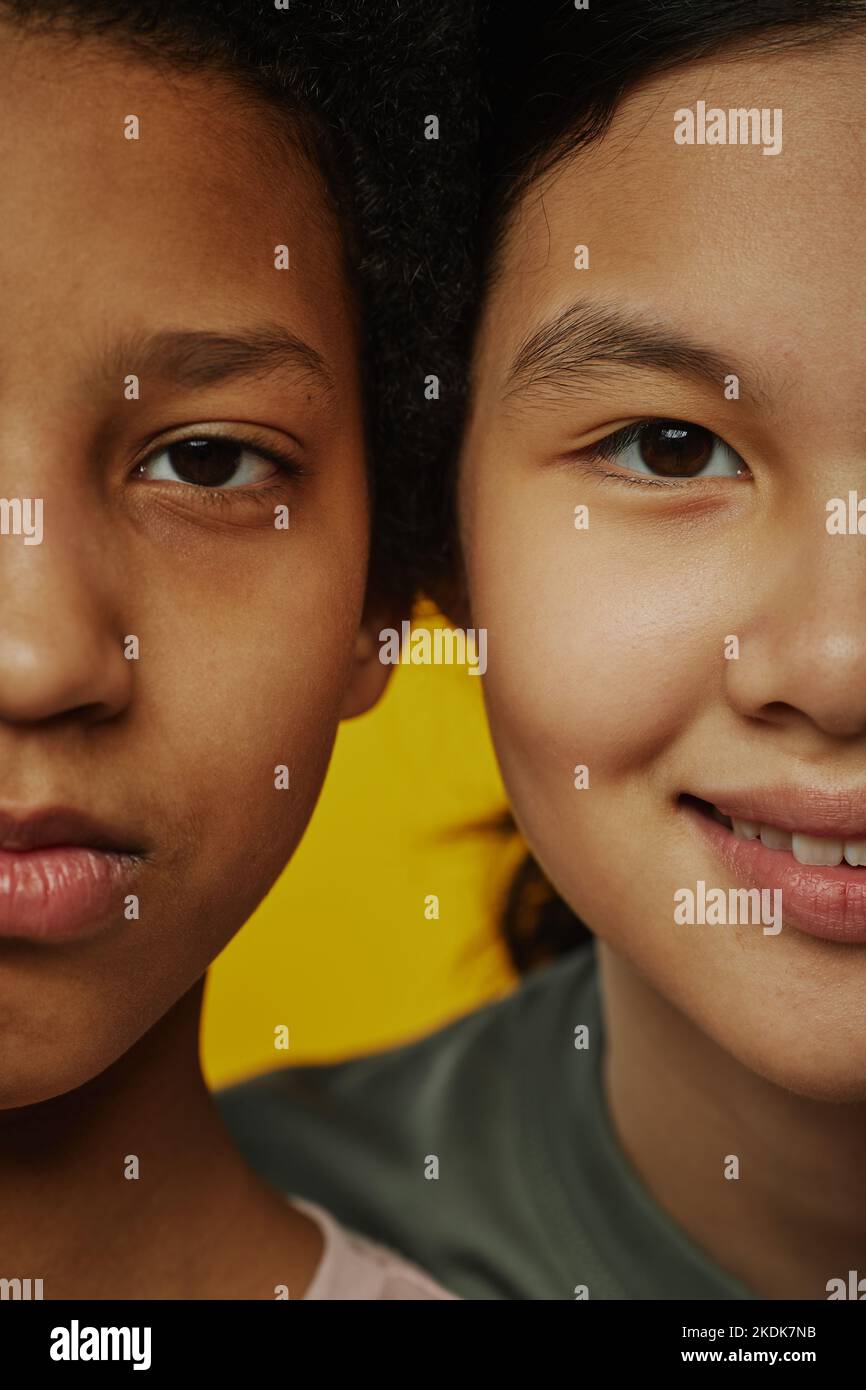 Close-up of half faces of two youthful multicultural girls with dark hair and brown eyes looking ...