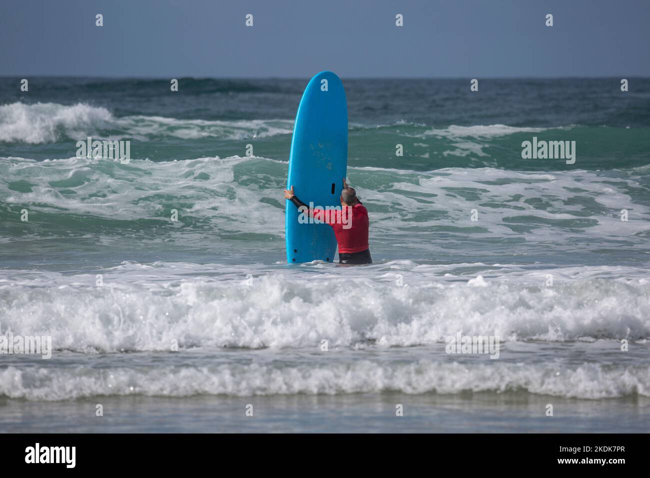 A surfer enters the water at A Lanzada beach with a blue apprentice surfboard Stock Photo - Alamy