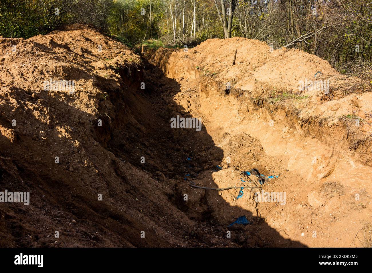 A deep trench dug in sandy soil in a forest area for laying engineering ...