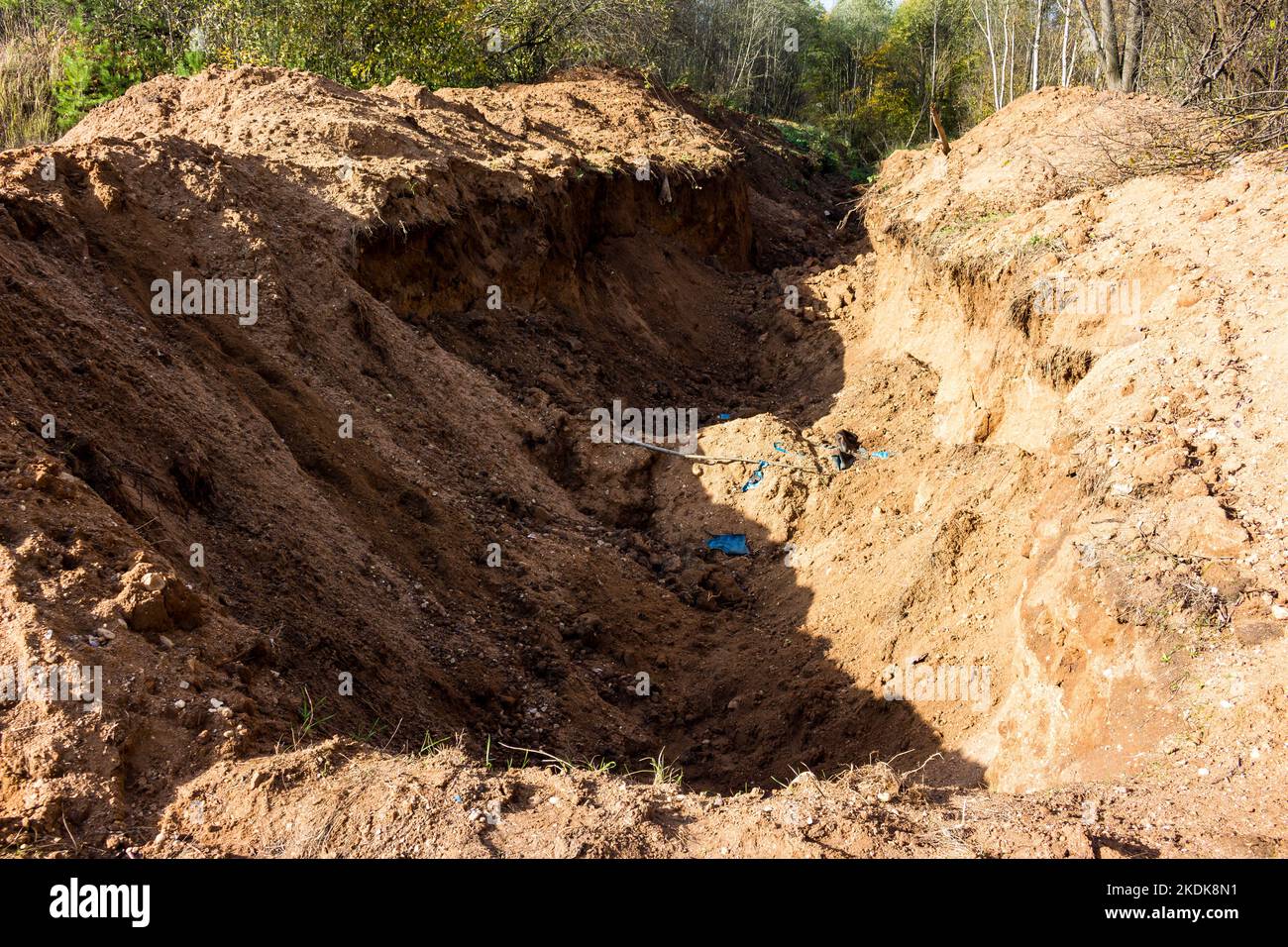 A deep trench dug in sandy soil in a forest area for laying engineering ...