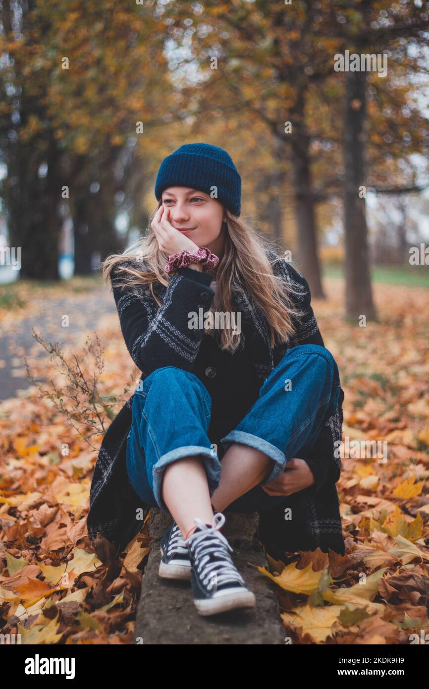 Smiling and happy brunette sitting in a pile of colourful leaves in a ...