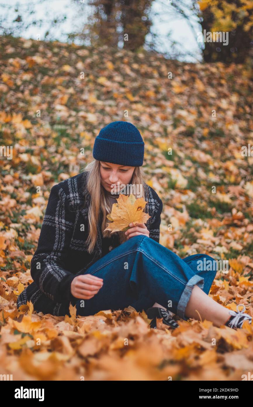 Smiling and happy brunette sitting in a pile of colourful leaves in a ...