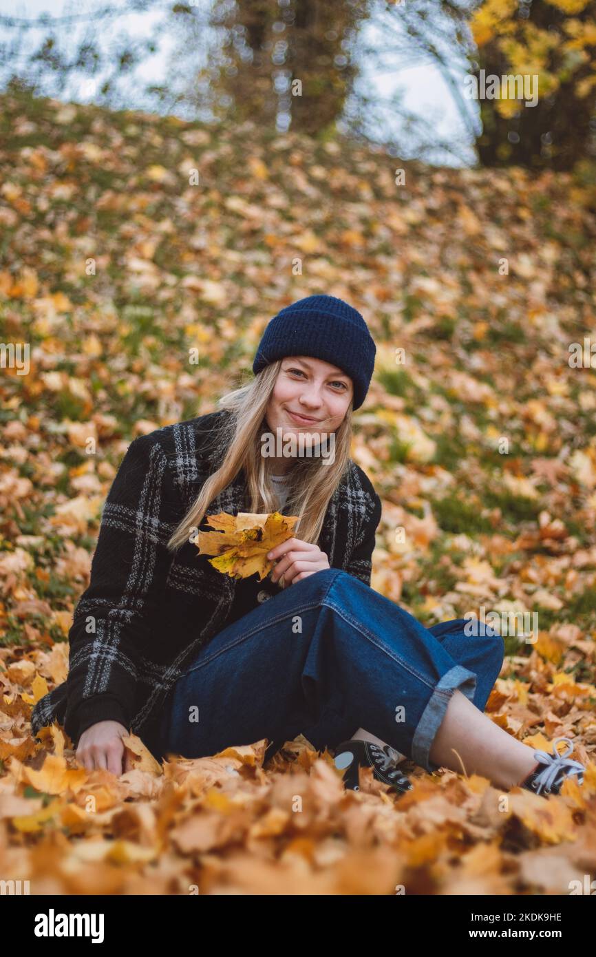 Smiling and happy brunette sitting in a pile of colourful leaves in a ...