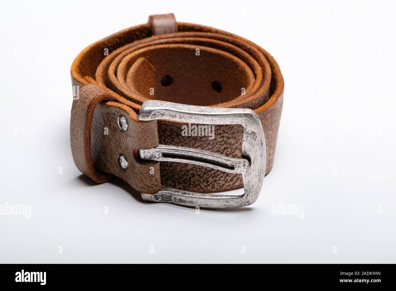 A rolled-up brown leather belt with a metal buckle on a white table ...