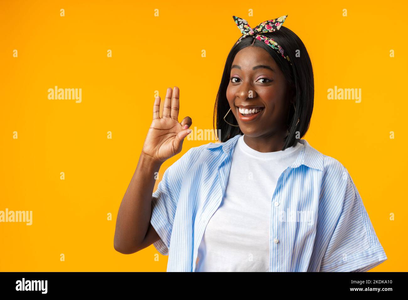 Smiling african woman showing ok sign and looking at camera over yellow ...