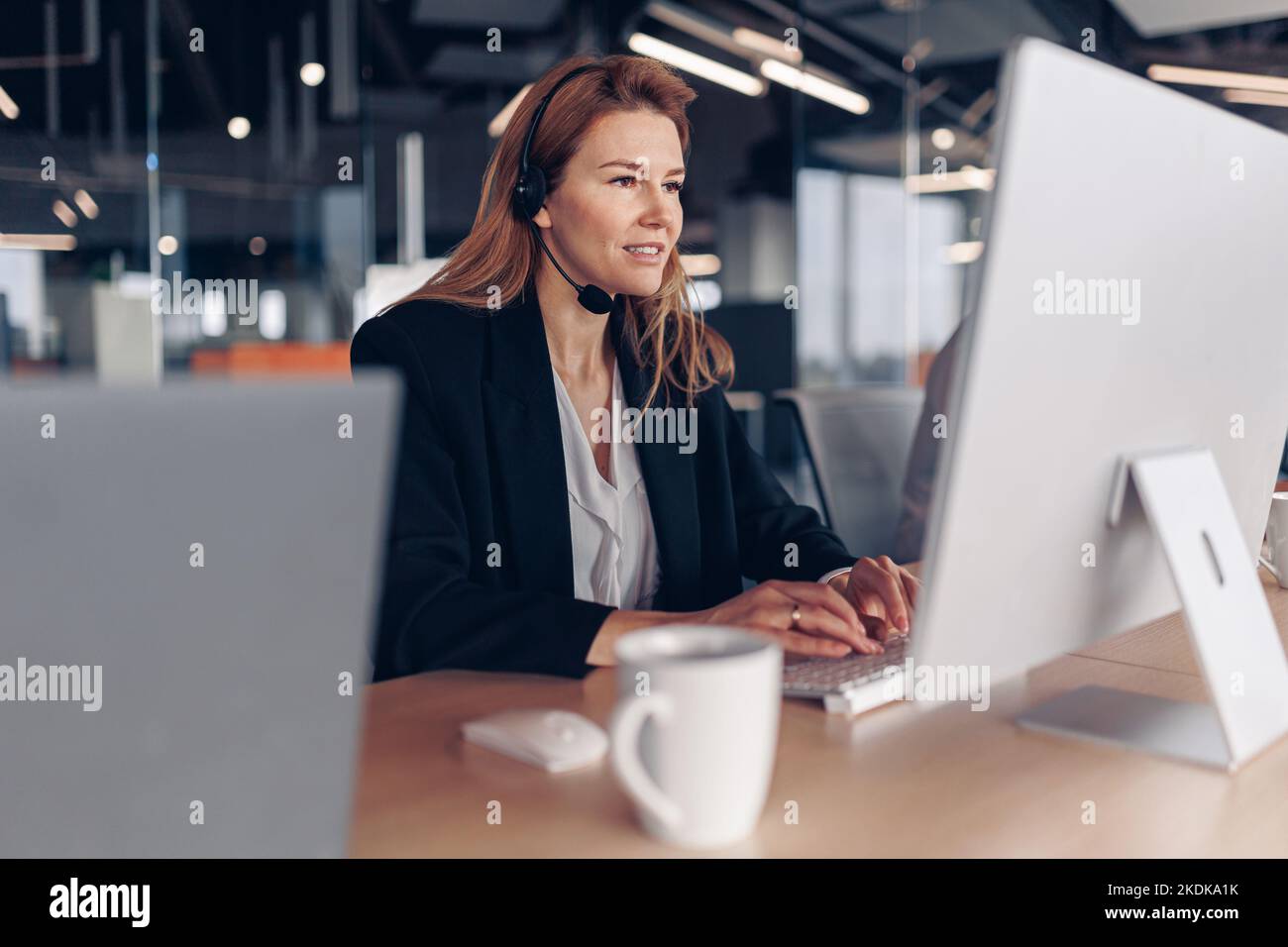 Pretty businesswoman in headphones working on computer while sitting in ...