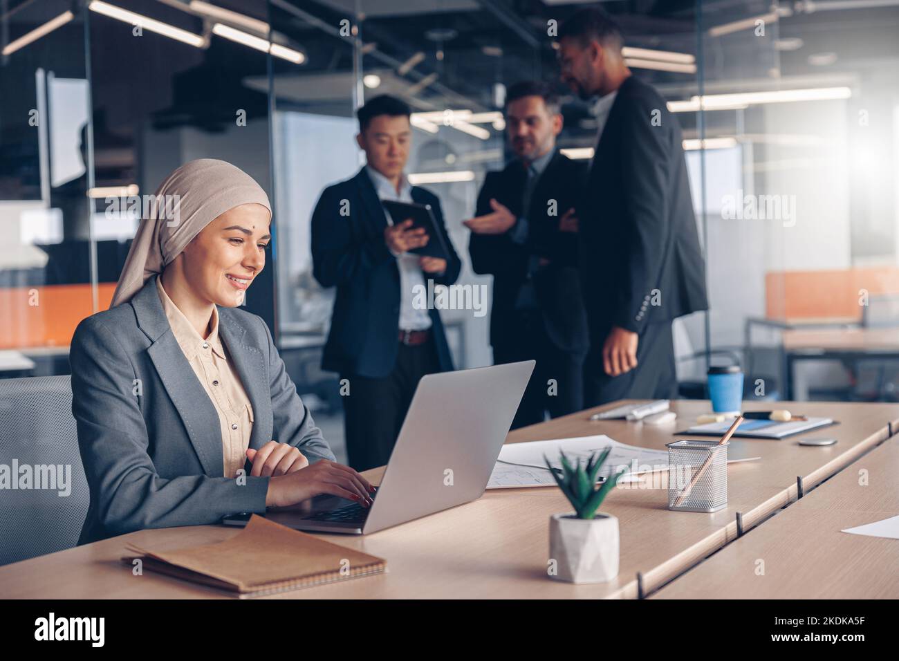 Smiling muslim businesswoman in hijab working on computer while sitting ...