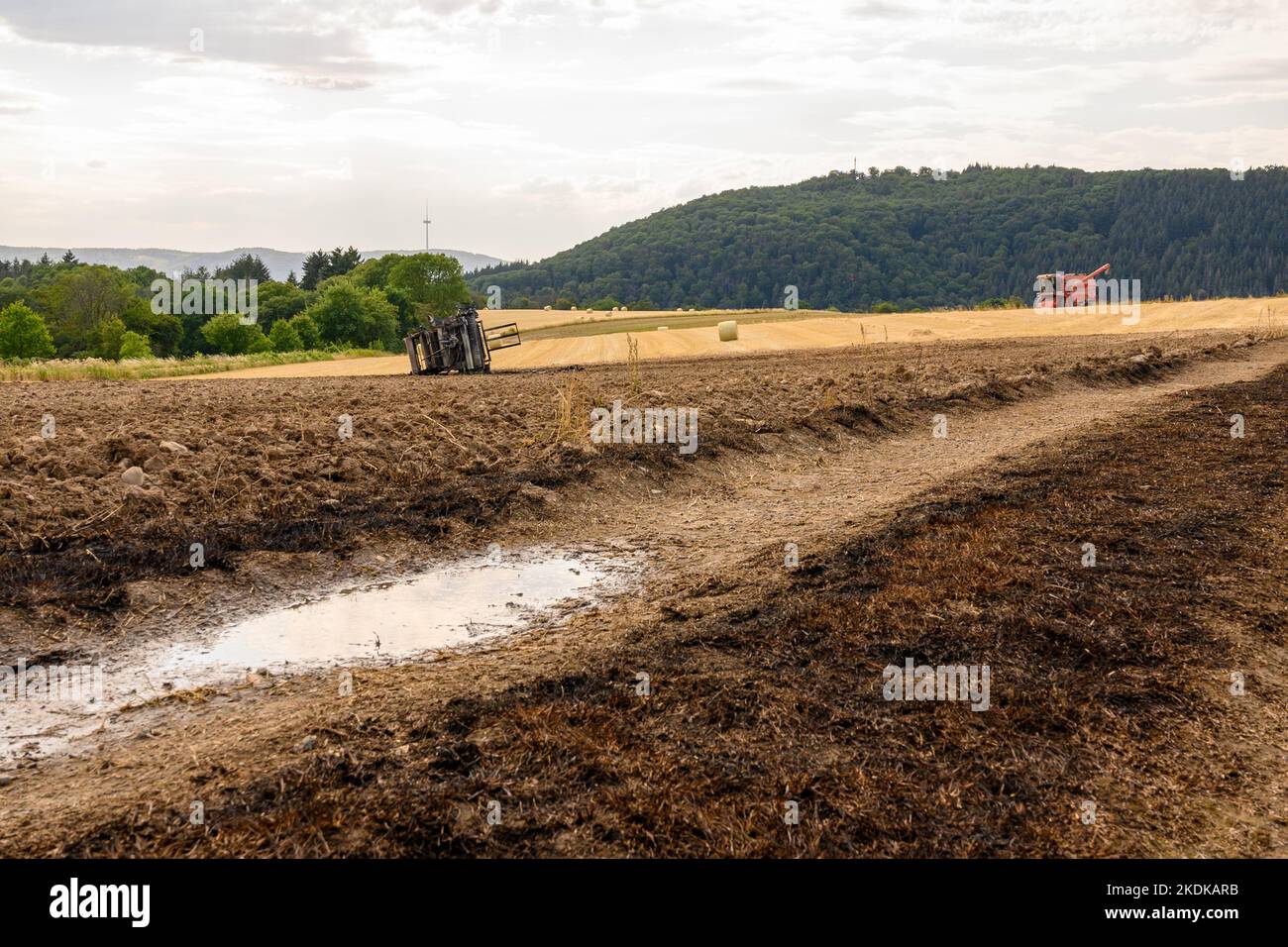 Burnt out hay baler in a field with puddle left after the fire was ...