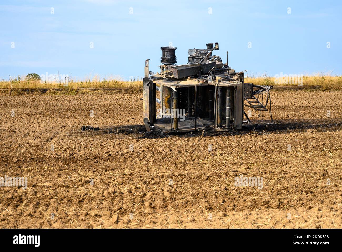 Top view of a burnt out hay baler on its side in a field with debris ...