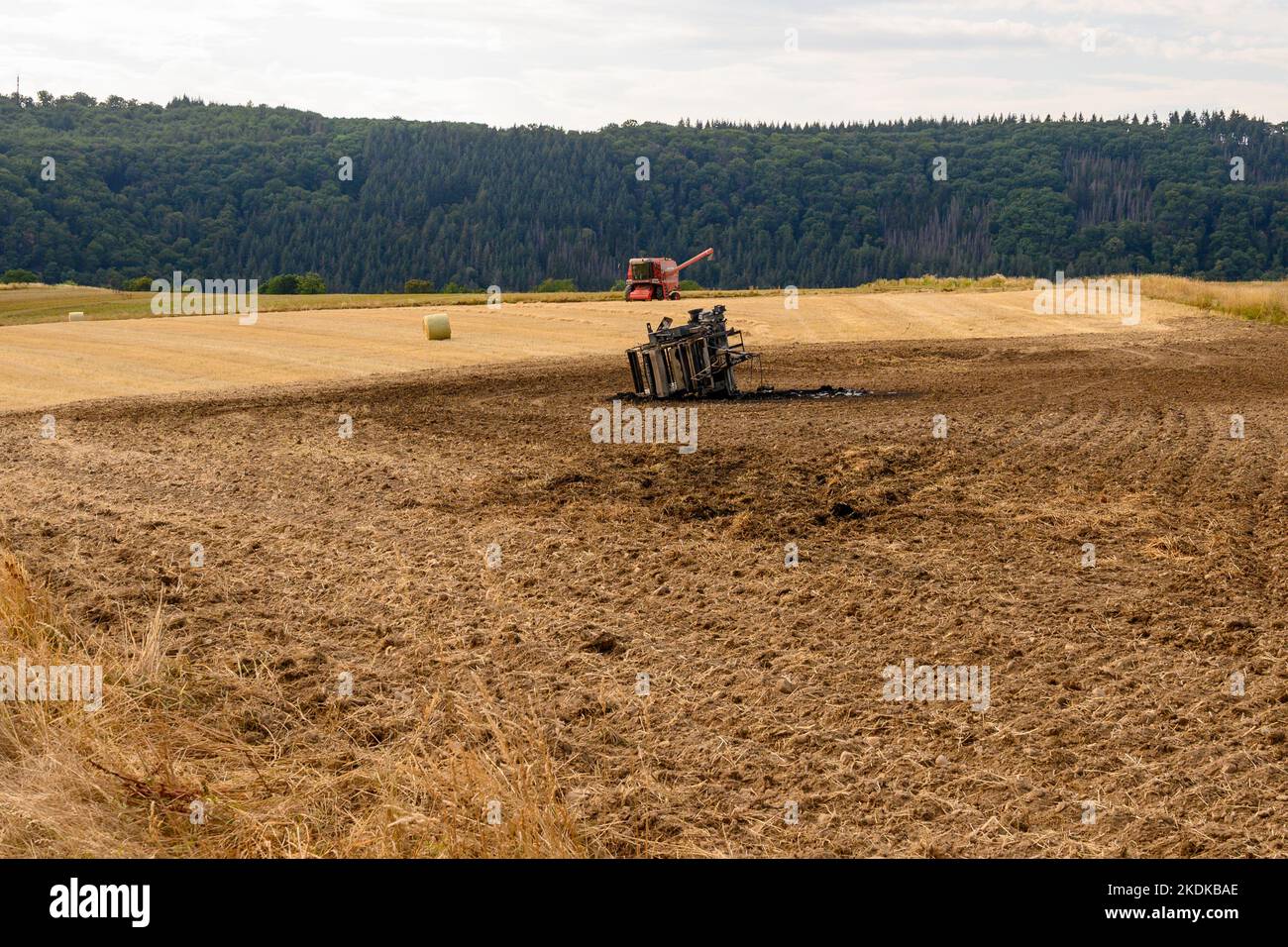 A burnt out hay baler lying on its side in a field with harvester and ...