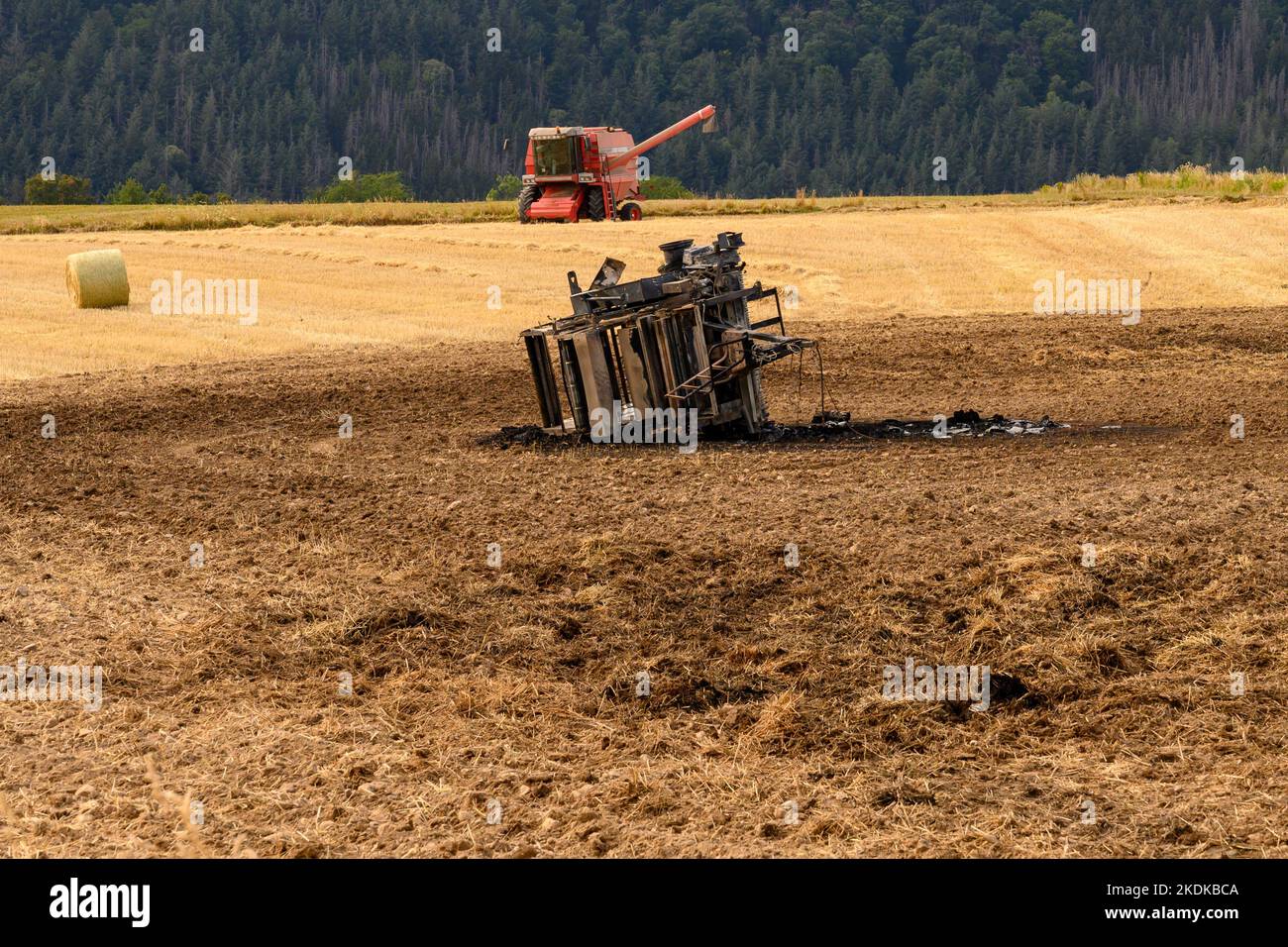 A burnt out hay baler in front of a combine harvester Stock Photo - Alamy