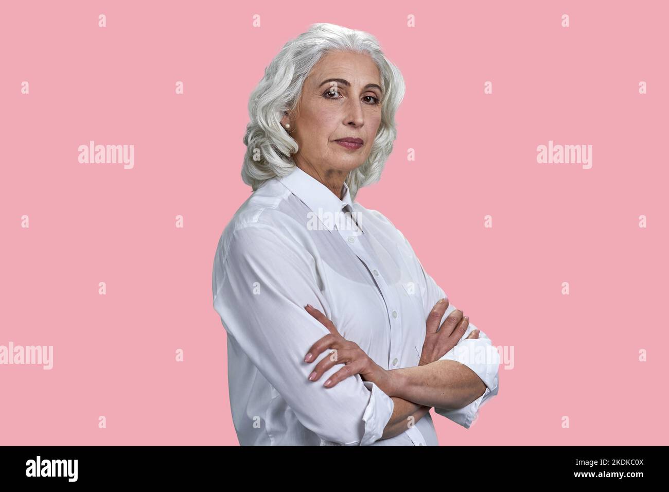 Portrait of aged gray-haired lady with crossed arms. Isolated on pink ...