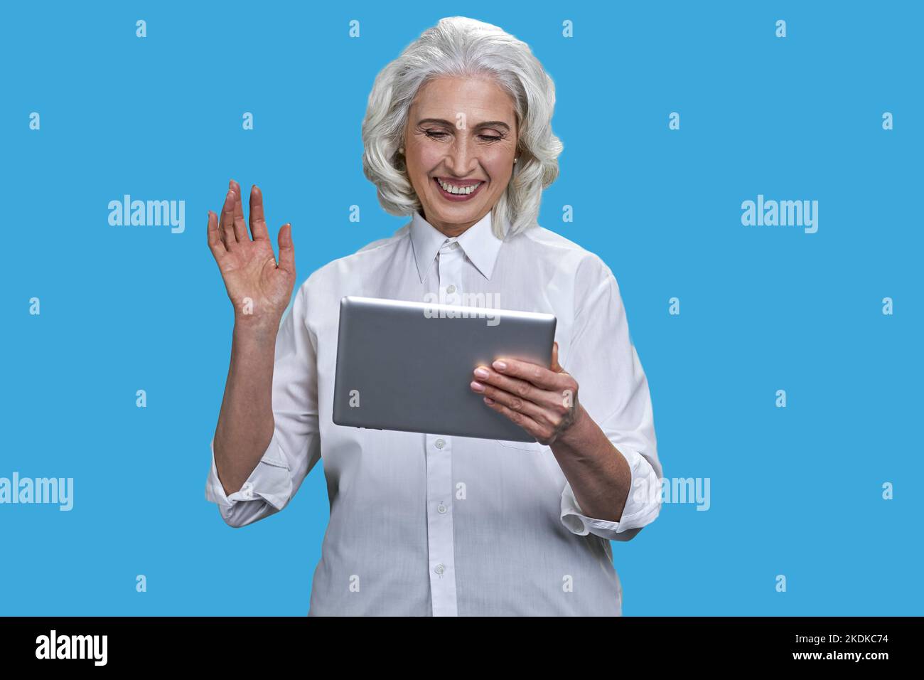Happy senior woman holding tablet pc and waving her hand to someone ...
