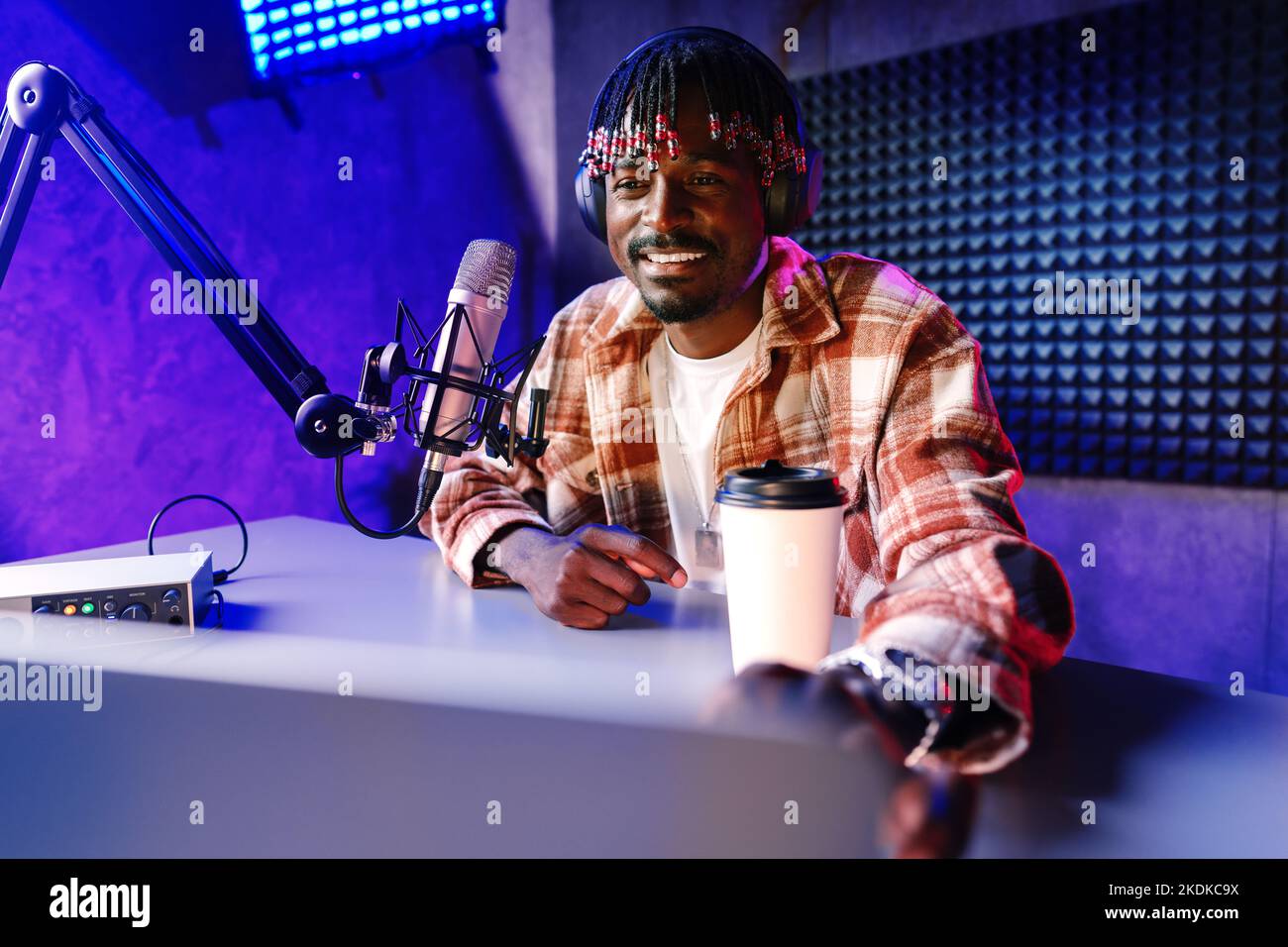 African radio host sitting at desk recording in studio with microphone ...