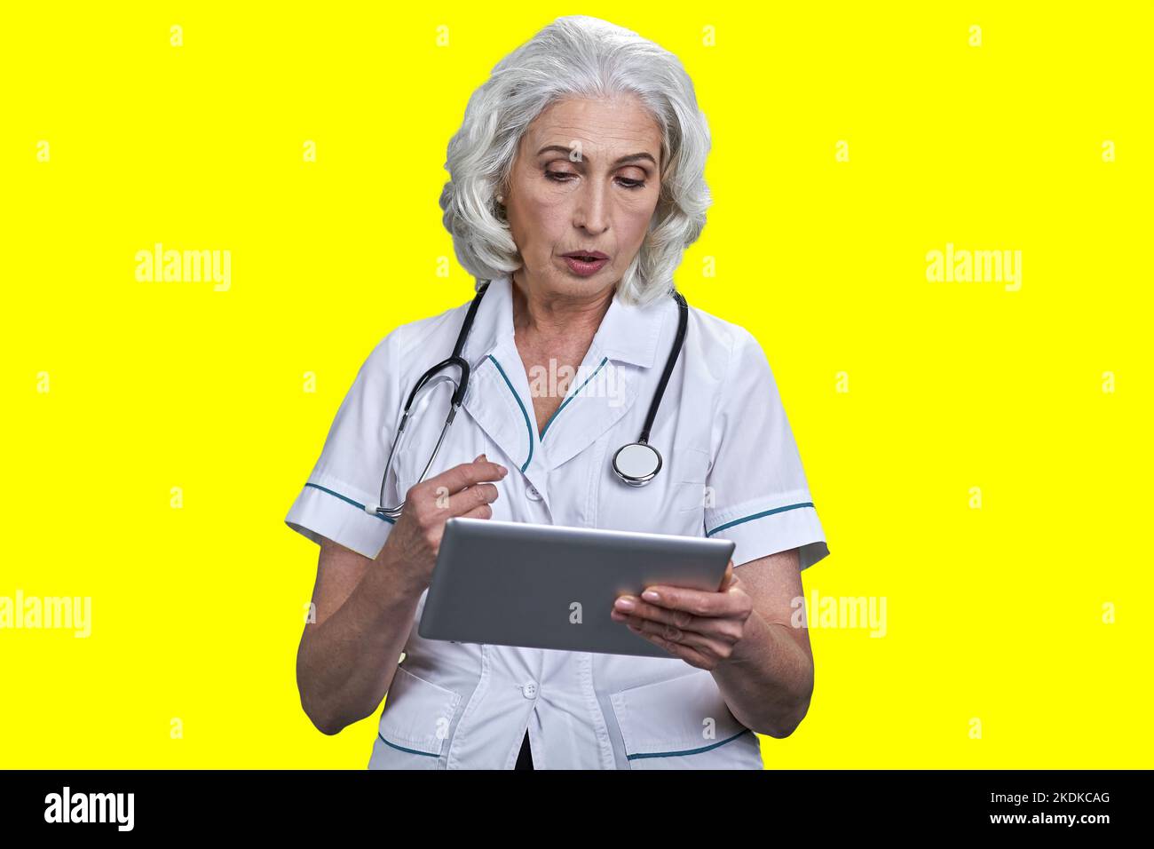 Serious aged gray-haired female doctor using tablet pc. Isolated on ...