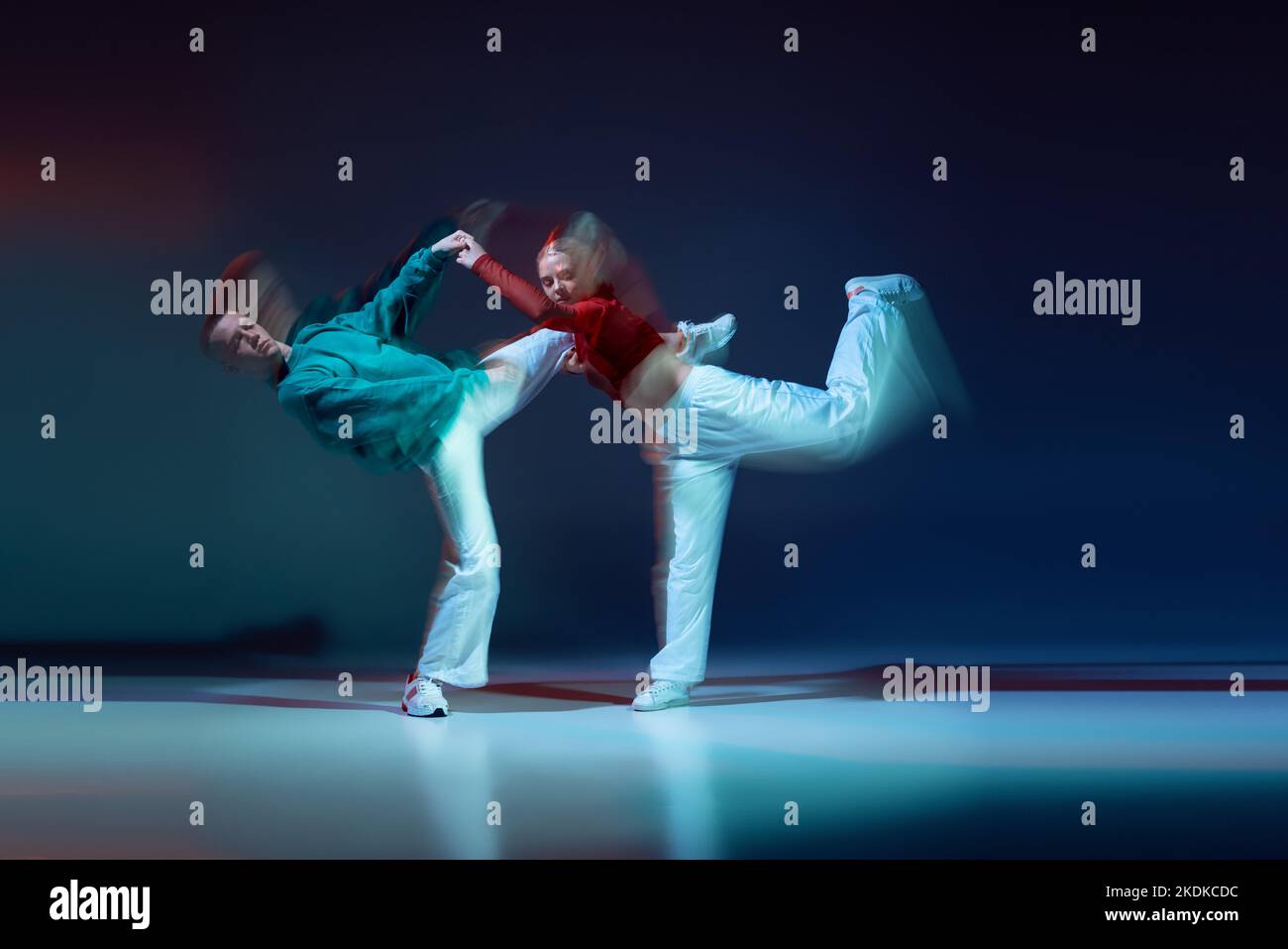 Portrait of young man and woman dancing hip-hop isolated over dark blue ...