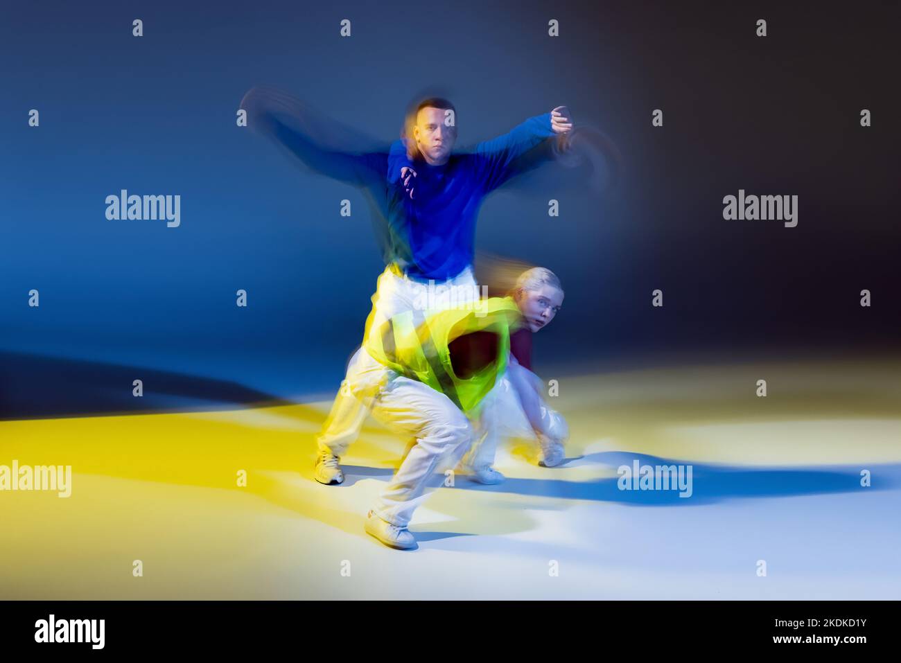 Portrait of young man and woman dancing hip-hop isolated over blue ...