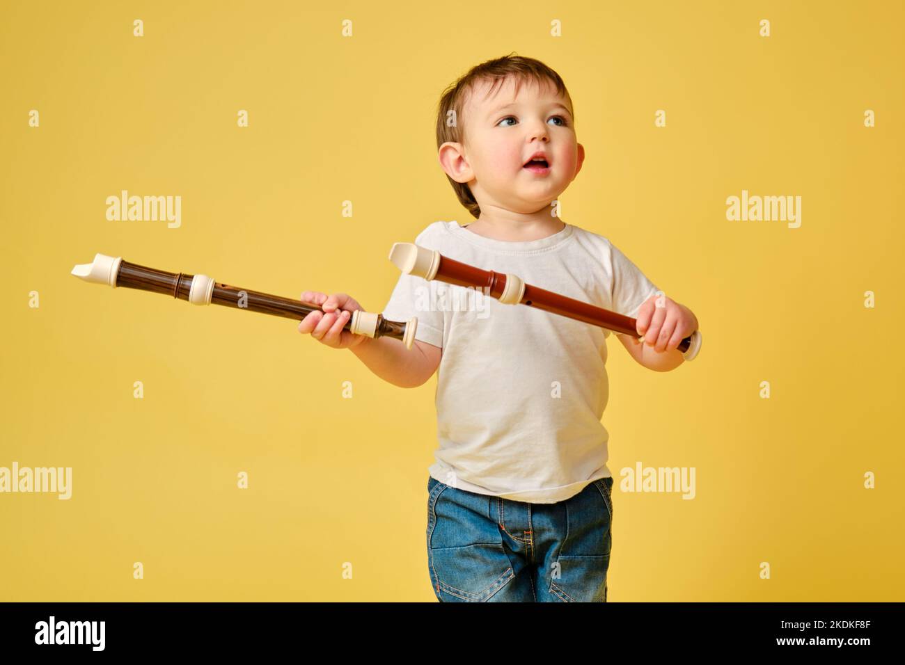 Toddler baby with a flute wind musical instrument on a studio yellow ...