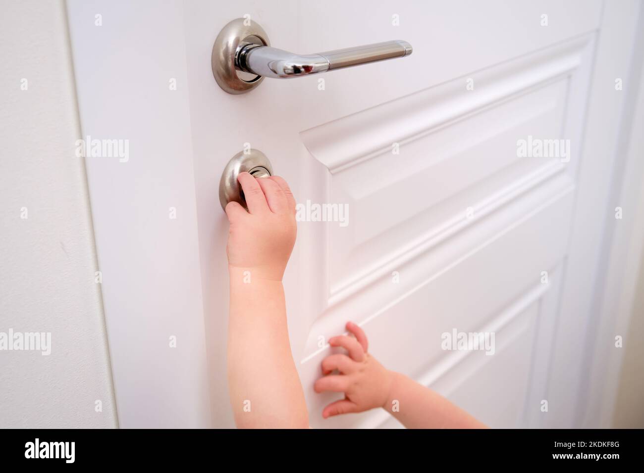 Toddler baby opens the lock, child s hand close-up. White wooden door ...