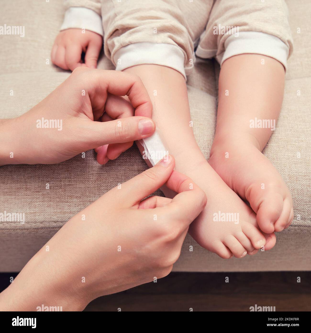 Mother woman sticks a medical adhesive plaster on the toddler baby leg ...
