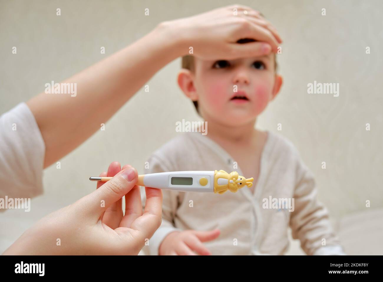 A mother woman measures the temperature of a sick toddler baby with a thermometer. Mom checks ...