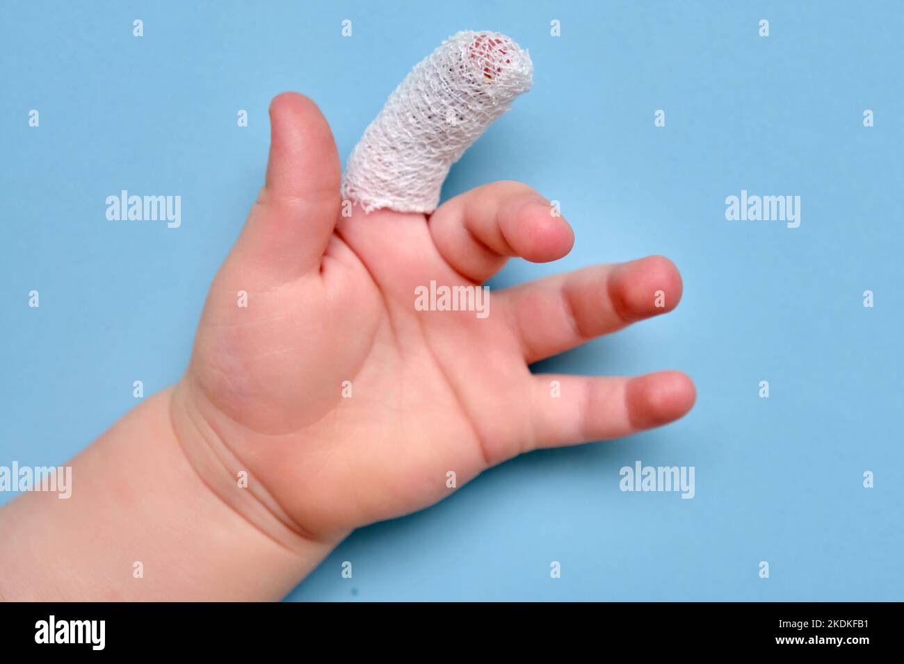 Baby s hand with a bandaged finger on a blue studio background, close ...